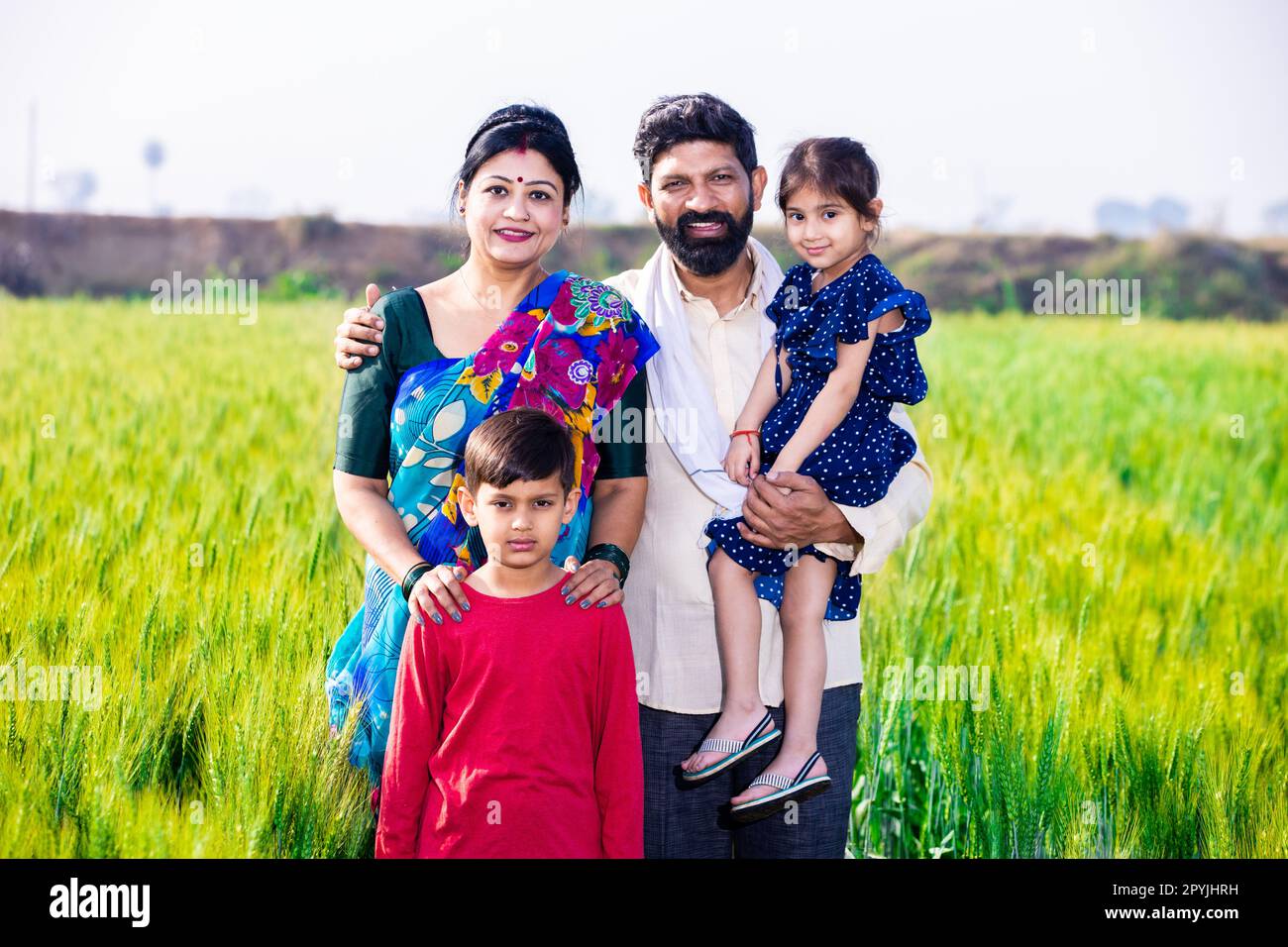Portrait of happy young indian farmer family standing at wheat ...