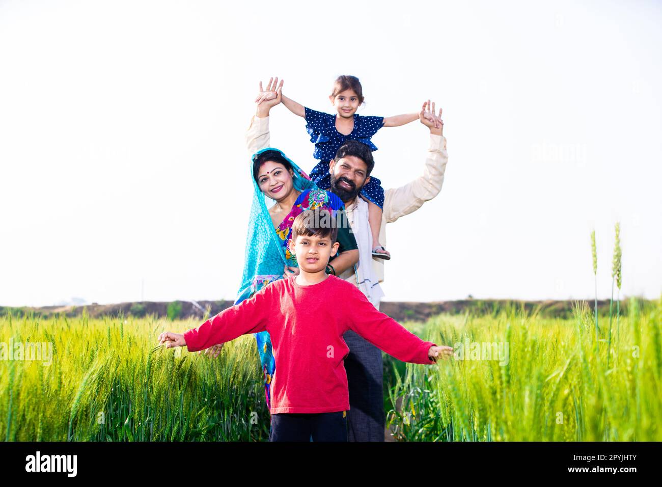 Portrait of happy young indian farmer family standing at wheat ...