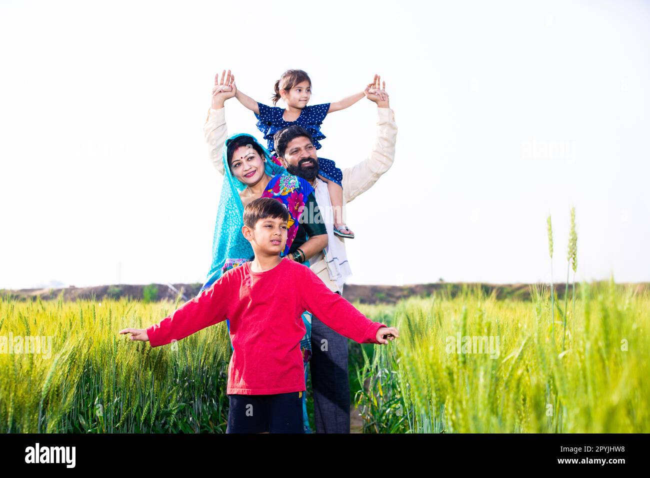 Portrait of happy young indian farmer family standing at wheat ...