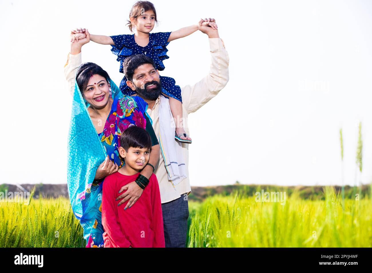 Portrait of happy young indian farmer family standing at wheat ...