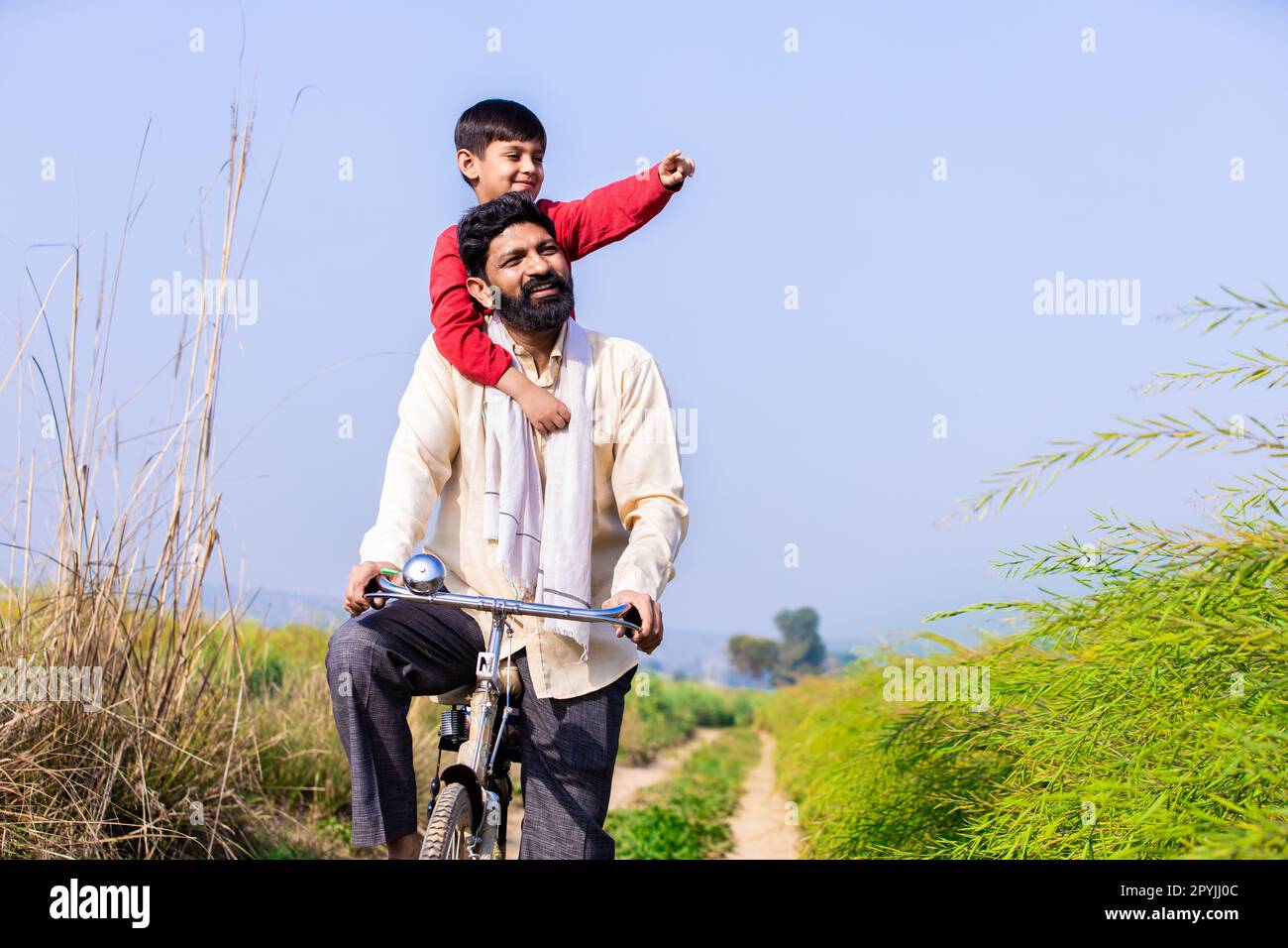 Rural Indian father and son riding bicycle in agricultural field in ...