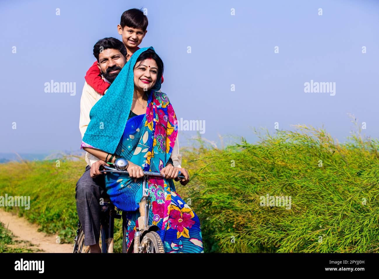 Rural Indian farmer family riding bicycle in agricultural field in ...