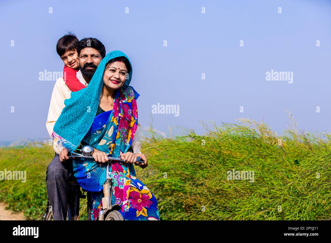 Rural Indian farmer family riding bicycle in agricultural field in ...