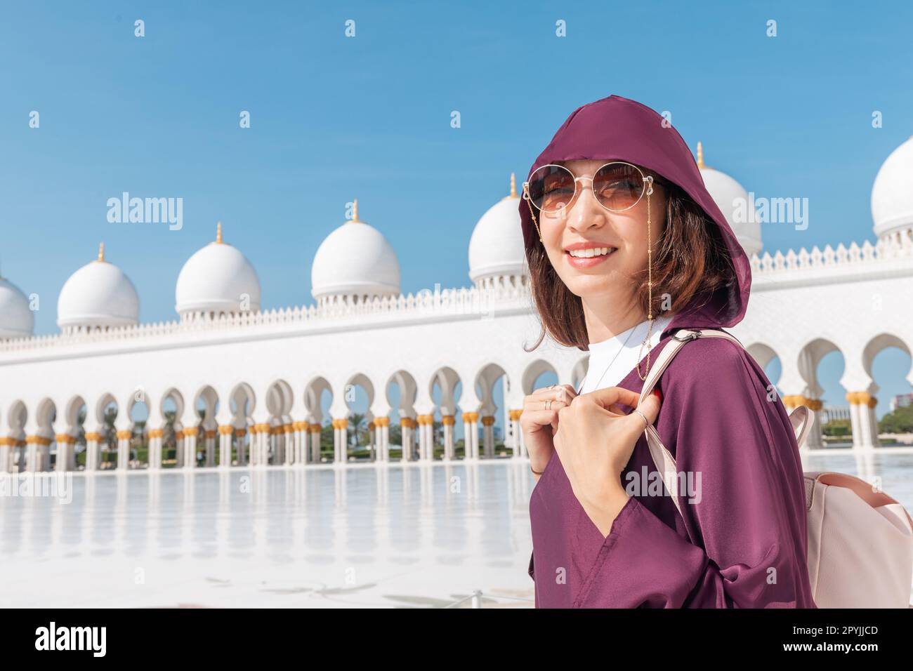 Against the backdrop of the awe-inspiring Sheikh Zayed Grand Mosque, a tourist girl in Abaya ...