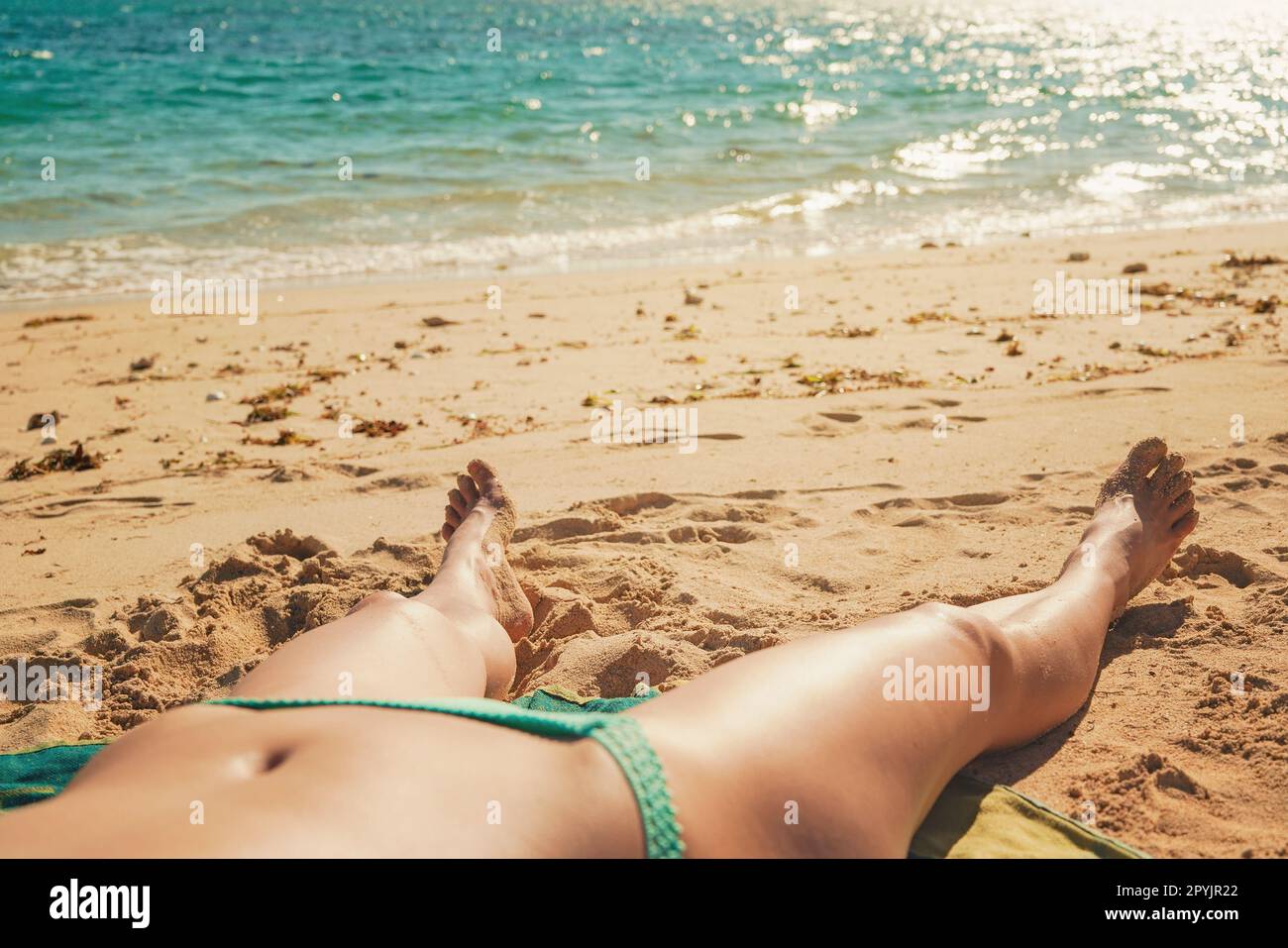 Young woman sunbathing on sandy beach, closeup detail to sand covered feet, calm sea background ...
