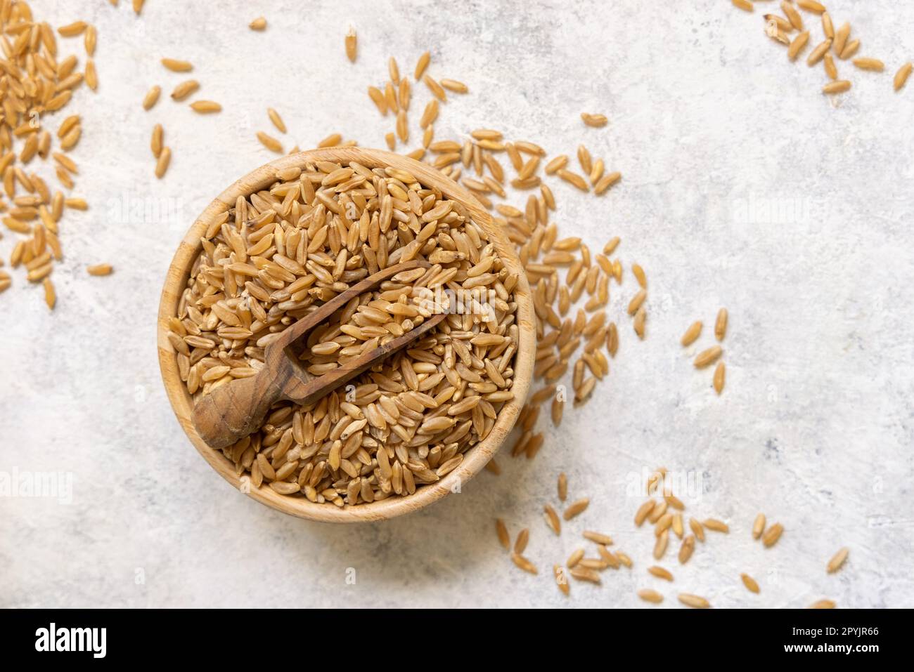 Bowl of raw dry rye grain with a wooden spoon on white table top view ...