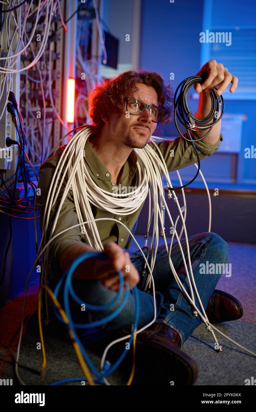 Crazy mad computer engineer wrapped in wires and cables in server room ...