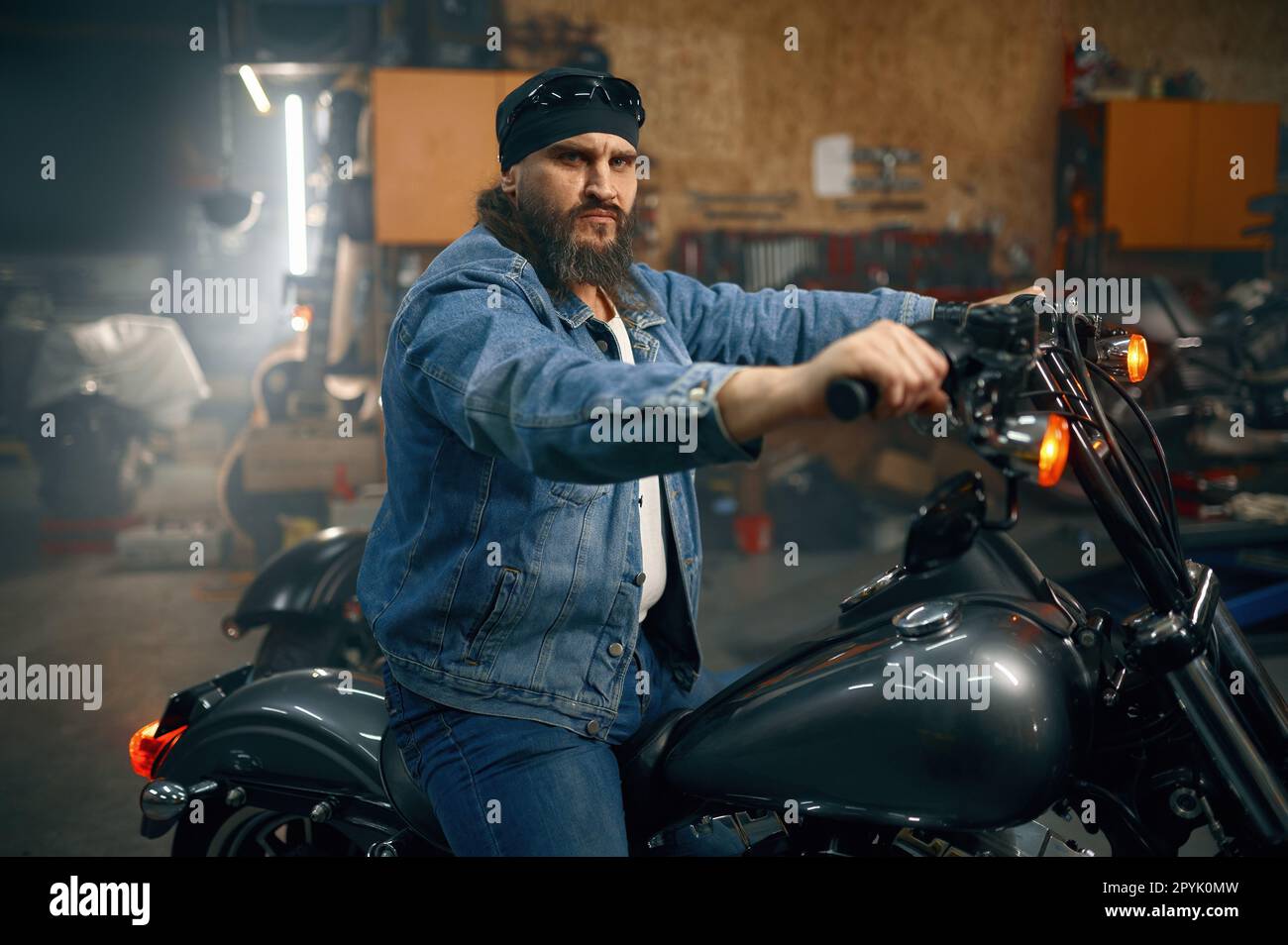 Portrait of mature bearded biker on motorcycle over garage interior ...