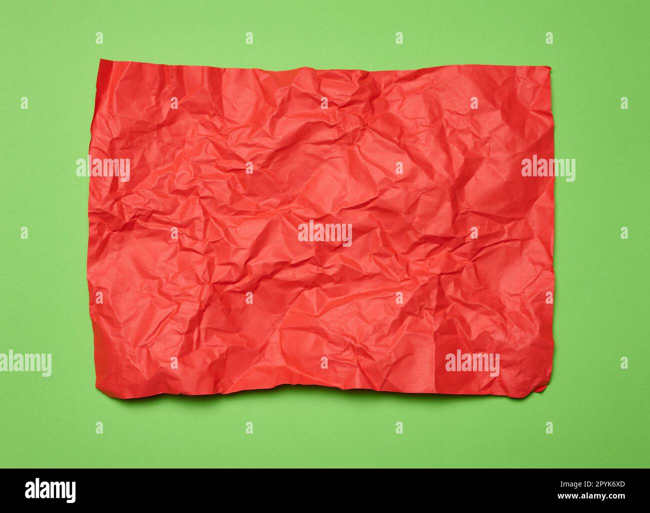 Crumpled rectangular sheet of red paper on a green background, top view ...