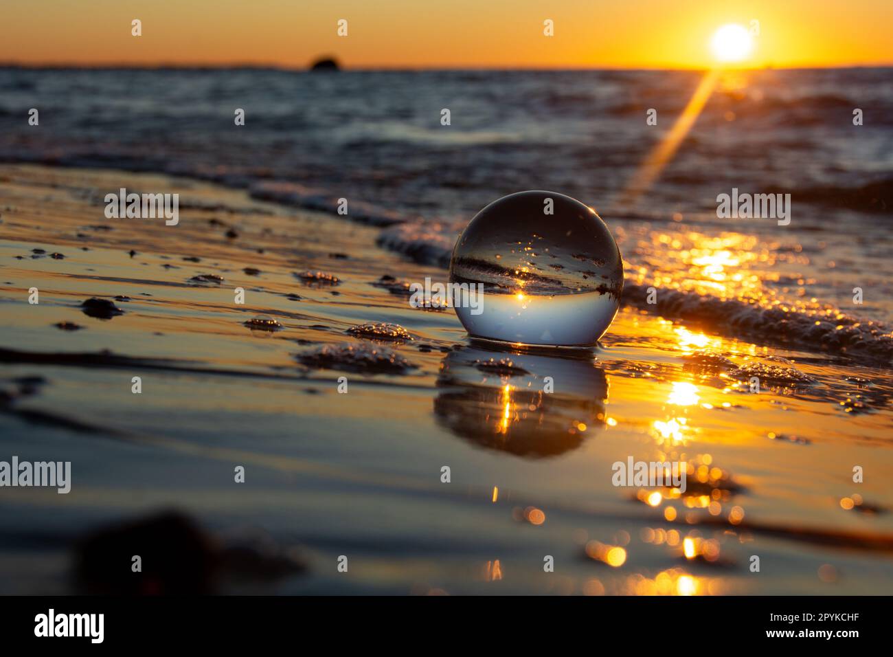 Beach and sea reflected in a sphere lying in the sand in the waves ...
