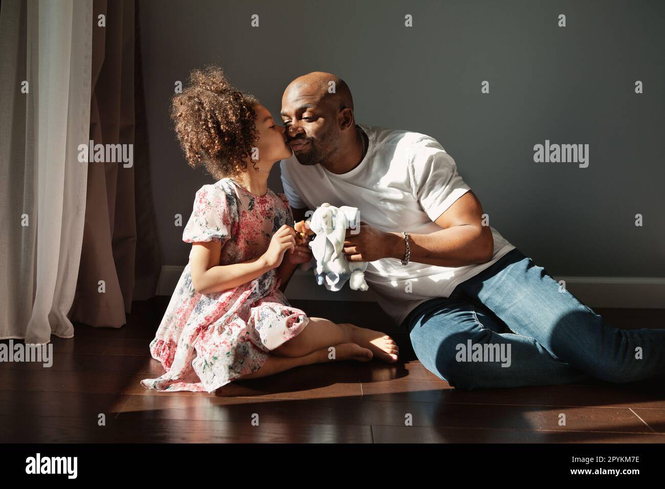 Happy African American father and his daughter playing toy together. Baby girl kissing dad ...