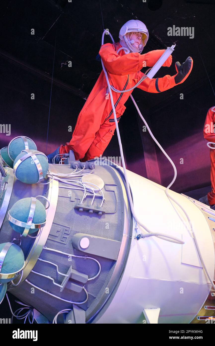 A Russian cosmonaut in an orange space suit floats above a capsule. A ...