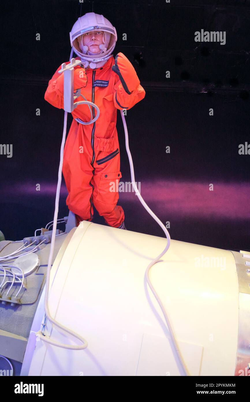 A Russian cosmonaut in an orange space suit floats above a capsule. A ...