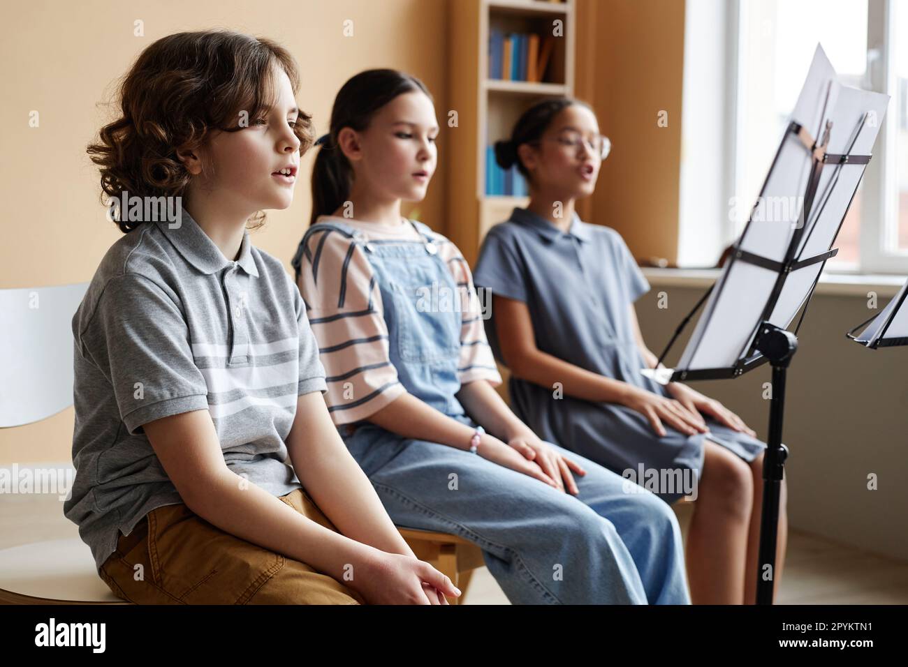 Group of children sitting in front of sheet music on stand and singing ...