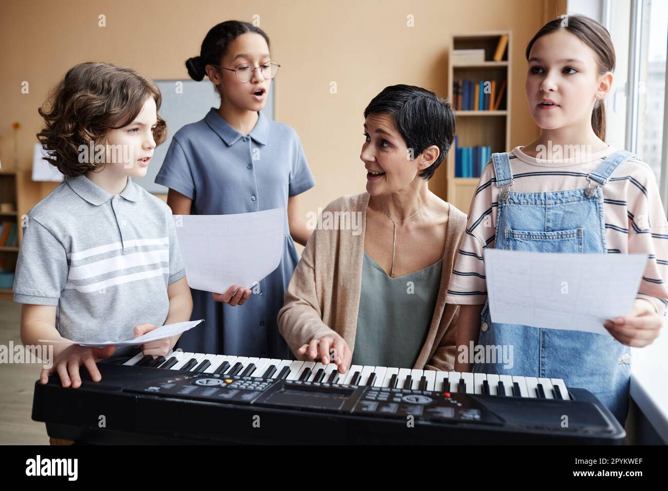 Music teacher singing songs together with children while playing piano ...