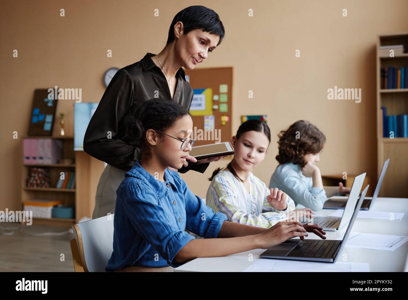 Group of school children using computers during study with teacher ...