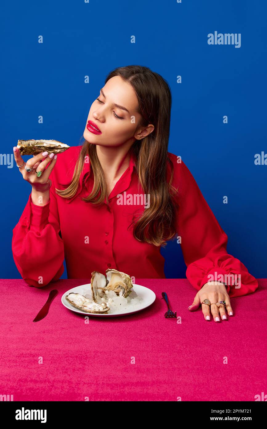 Portrait of charming woman, girl eating oyster over blue studio ...