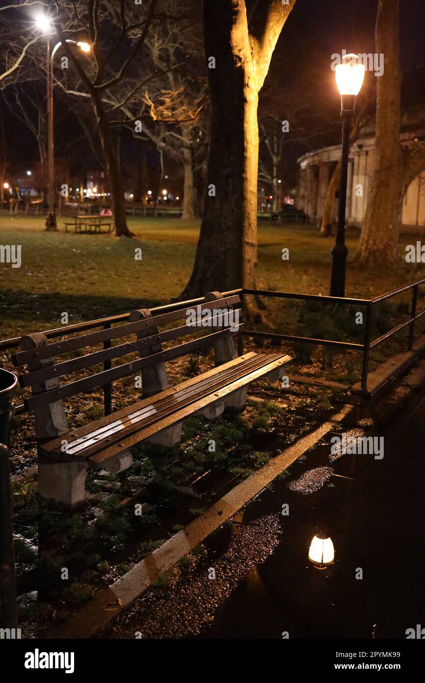 An outdoor park bench illuminated by a streetlight at night Stock Photo ...