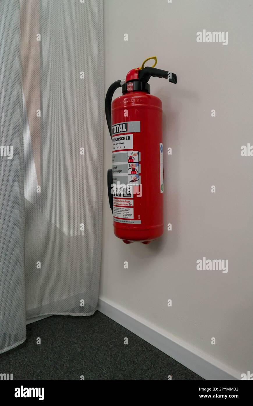 A red fire extinguisher standing in front of a plain white curtain ...