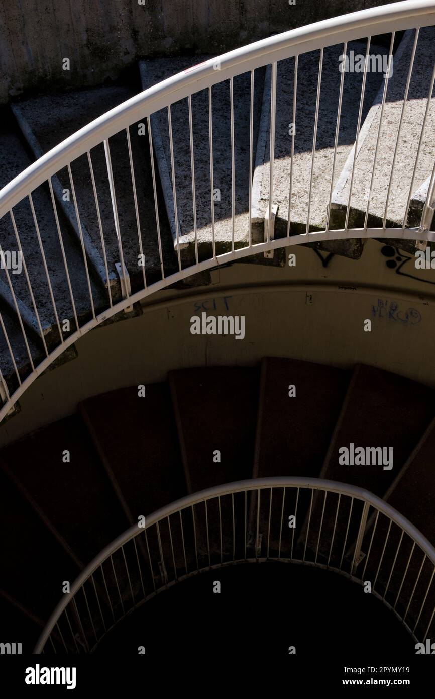 A concrete and metal spiral staircase descending down into a dark stair ...