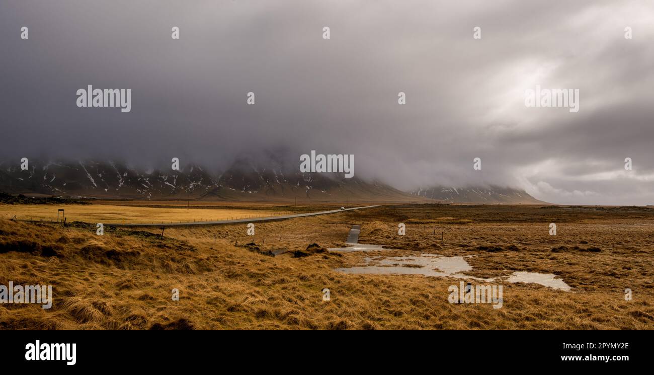 Icelandic countryside with moss on land, empty road and snow mountains ...
