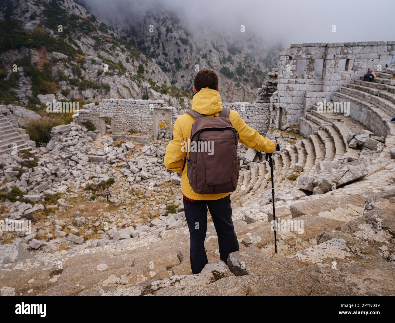 Autumn walk , man in yellow jacket looks at the ancient amphitheatre in ...