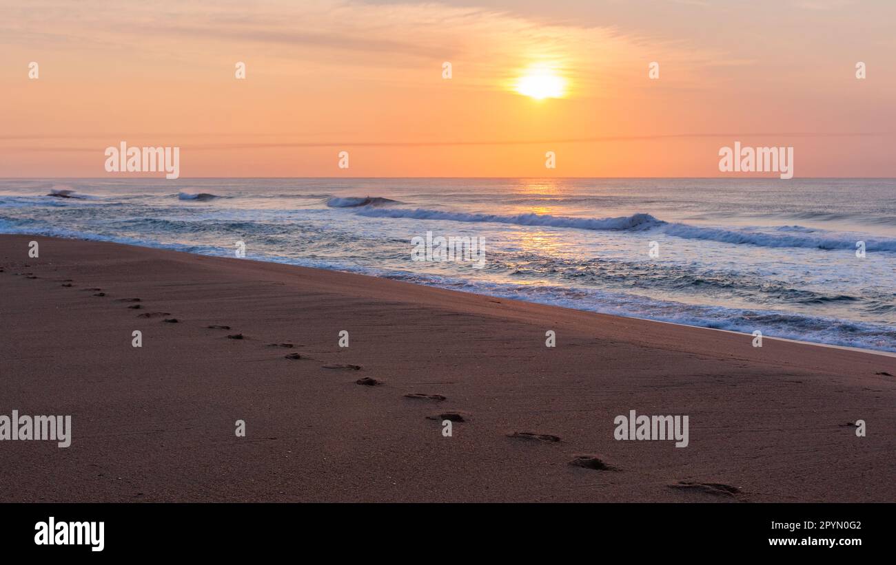 Beach sand footprints shoreline ocean waves wash with sun haze on the ...