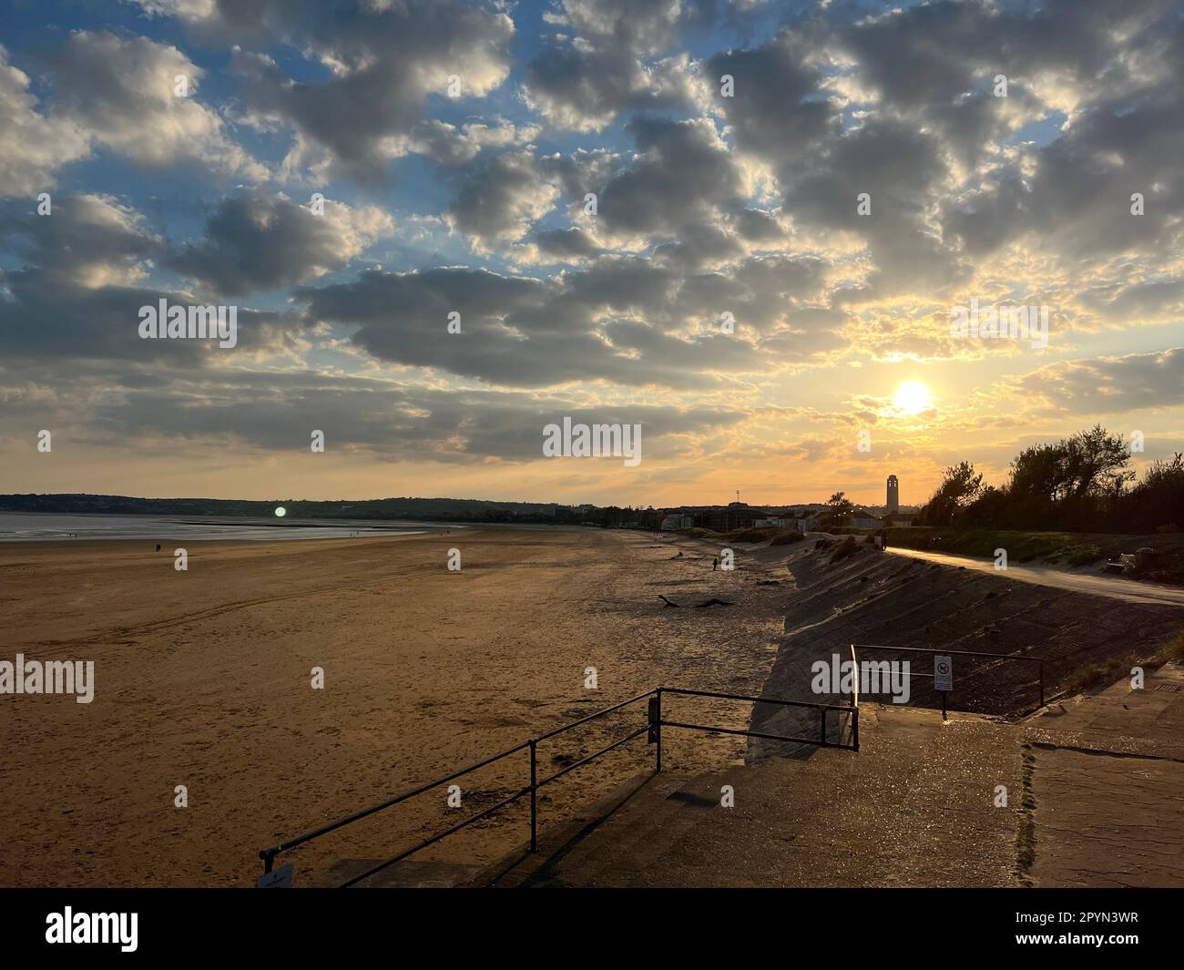 A sandy beach with a set of wooden stairs, surrounded by a cloudy sky ...