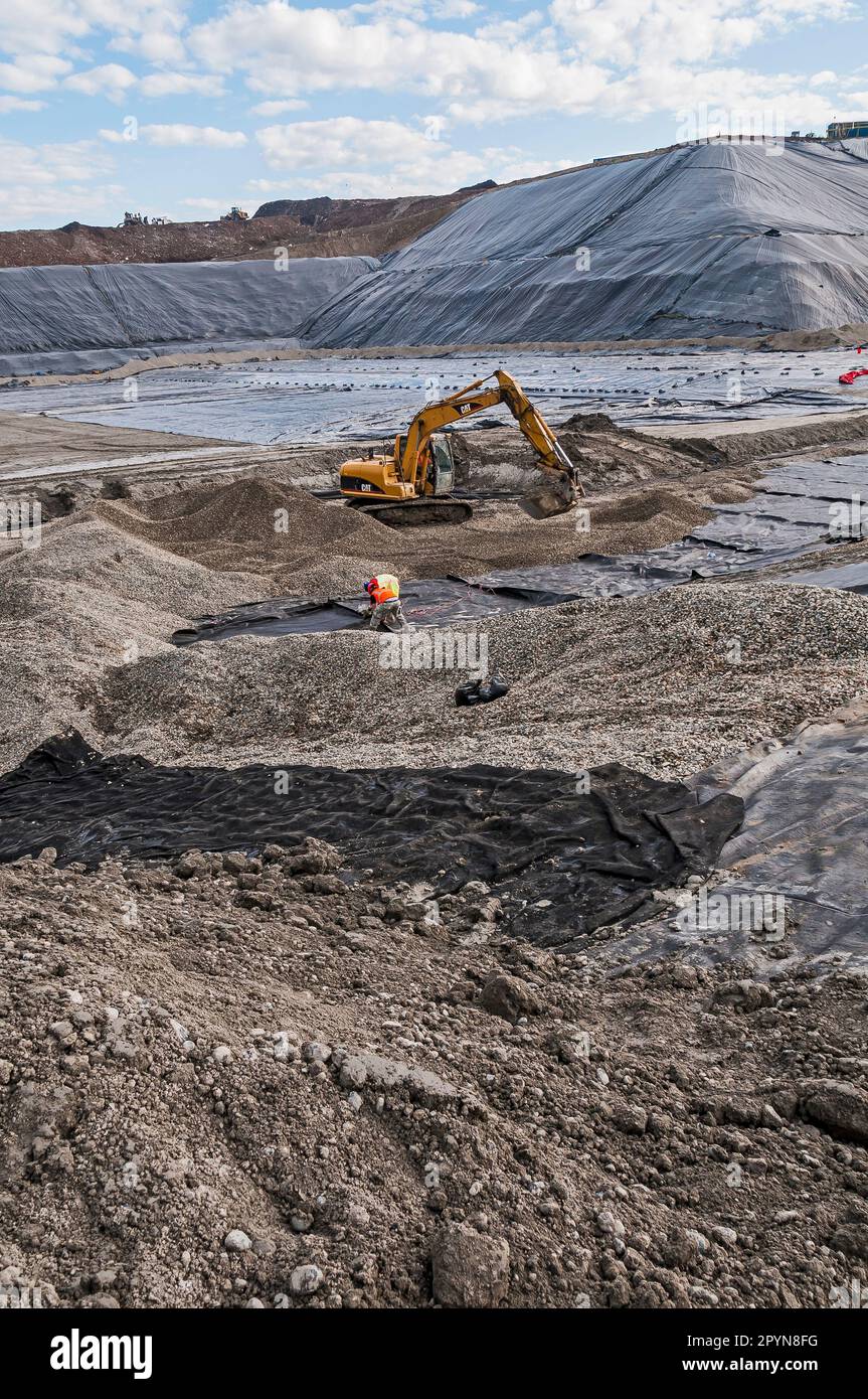 Workers and a power shovel work to excavate and install geomembrane in ...