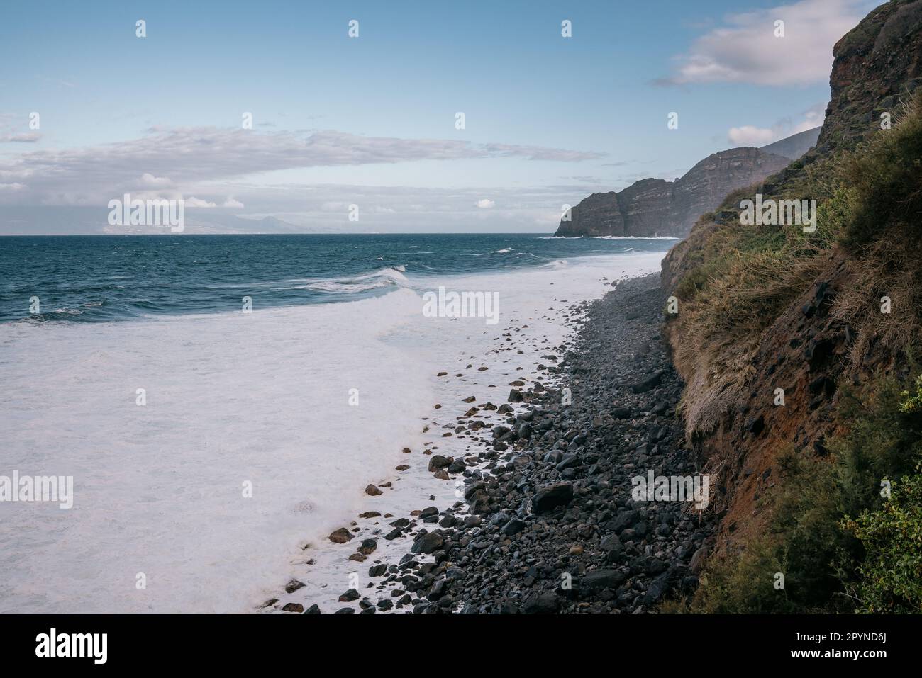 An idyllic landscape featuring a rocky shoreline and a large cliff ...