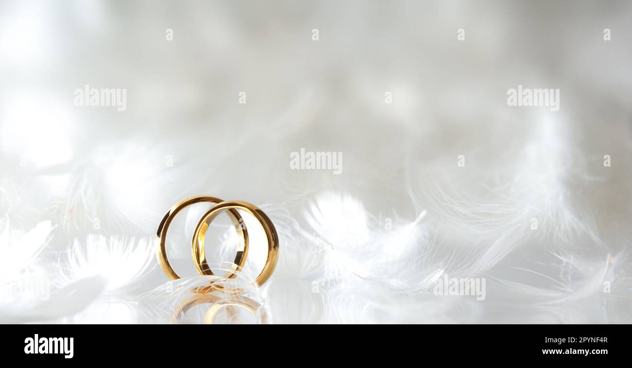 Detail of two gold rings standing on a reflective base and many white ...