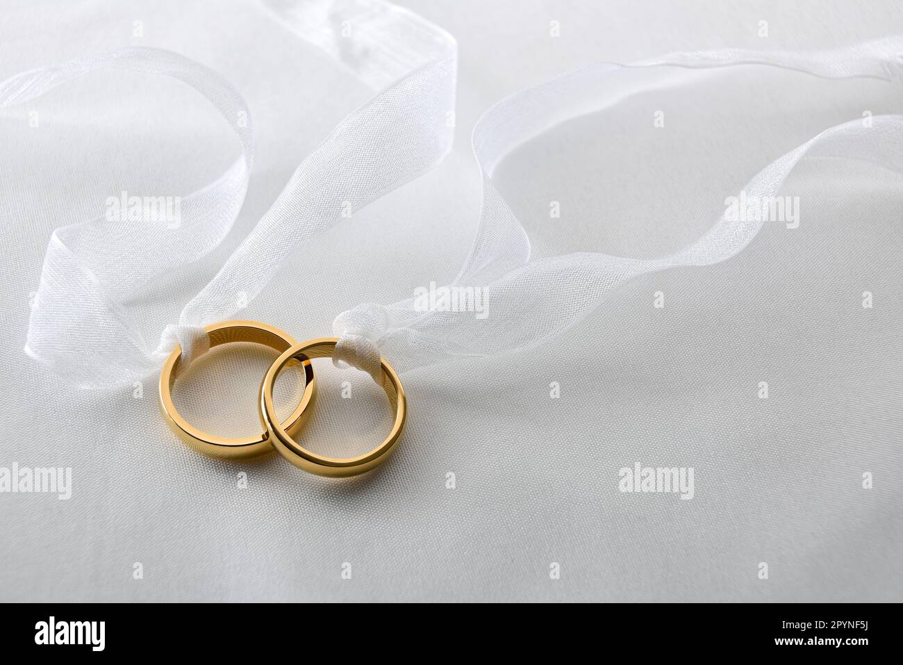 Detail of two gold wedding rings with white ribbon tied on white fabric ...