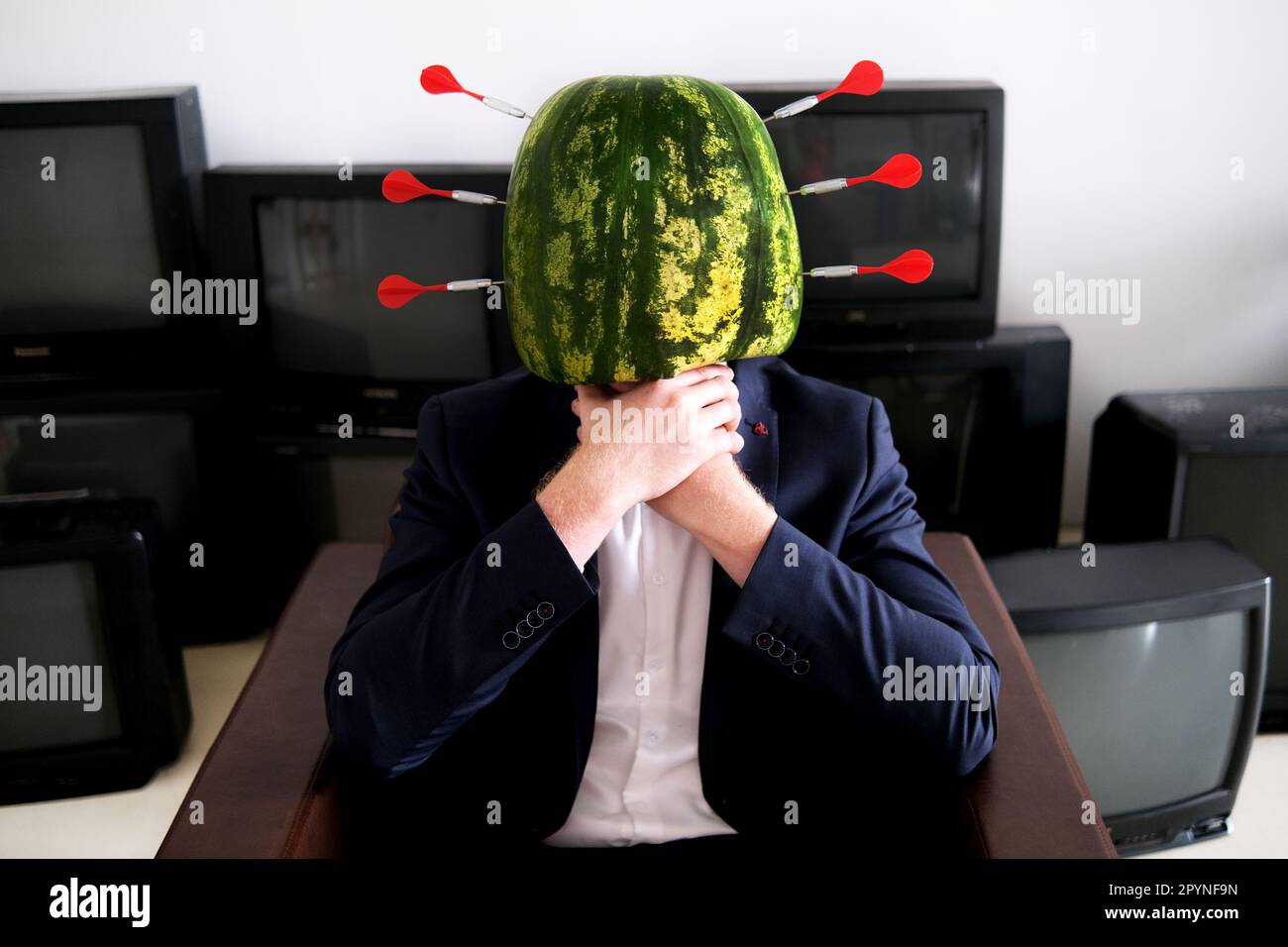 A man with a watermelon-shaped head. Darts are inserted into a ...