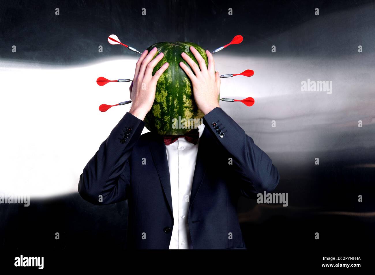 A man with a watermelon-shaped head. Darts are inserted into a ...