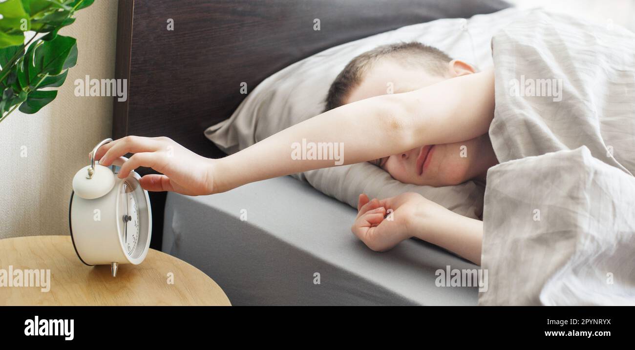 boy lying on bed and stopping alarm clock in morning. childs hand ...