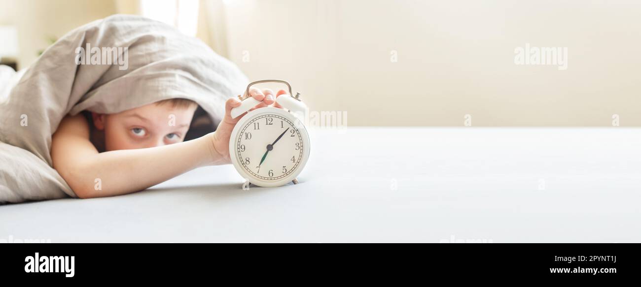 boy lying on bed and stopping alarm clock in morning. childs hand ...