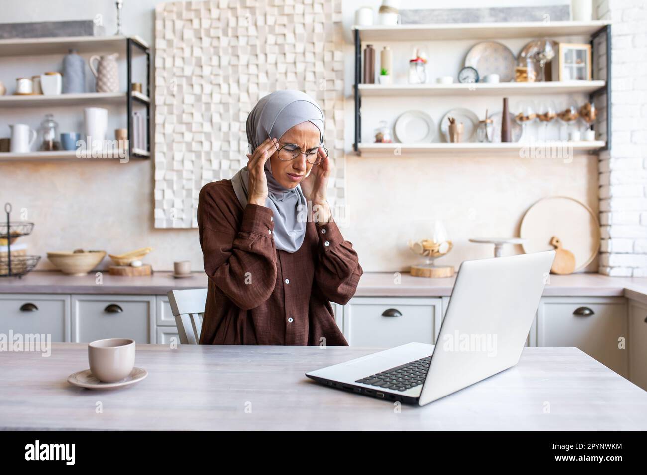 Tired young Muslim student in hijab studying remotely from home using ...