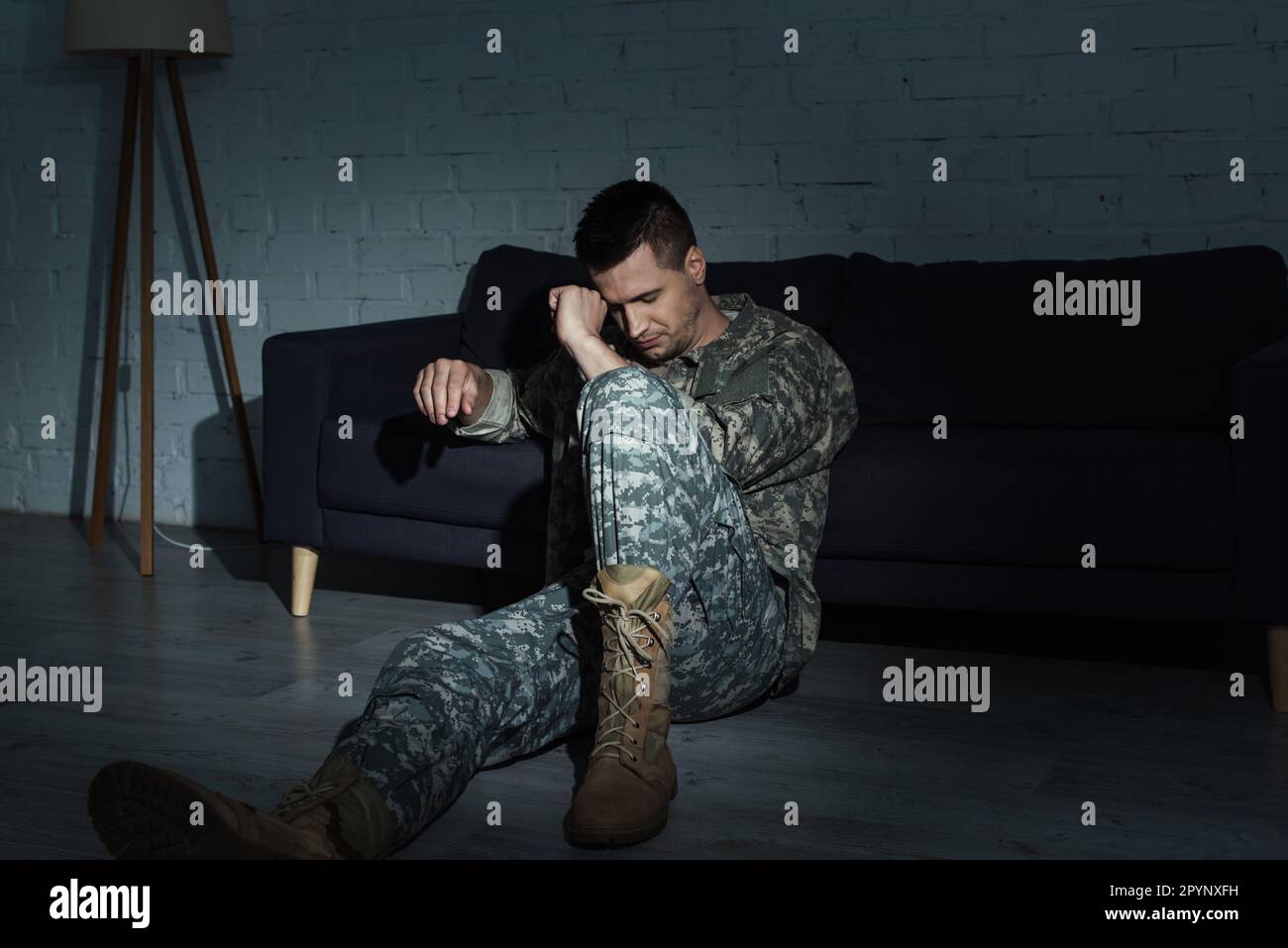 depressed serviceman in military uniform sitting on floor while ...