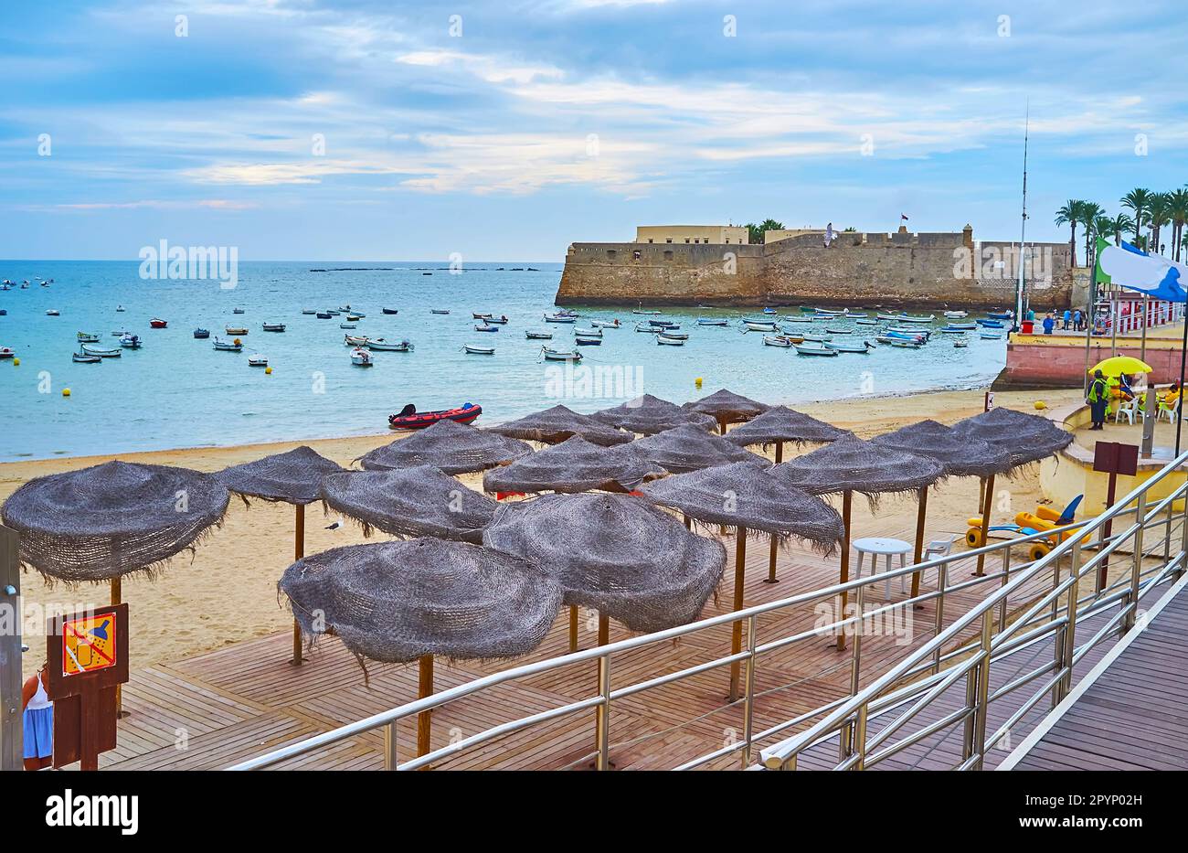 the straw sunshades on La Caleta beach, small fishing boats, rocking on ...