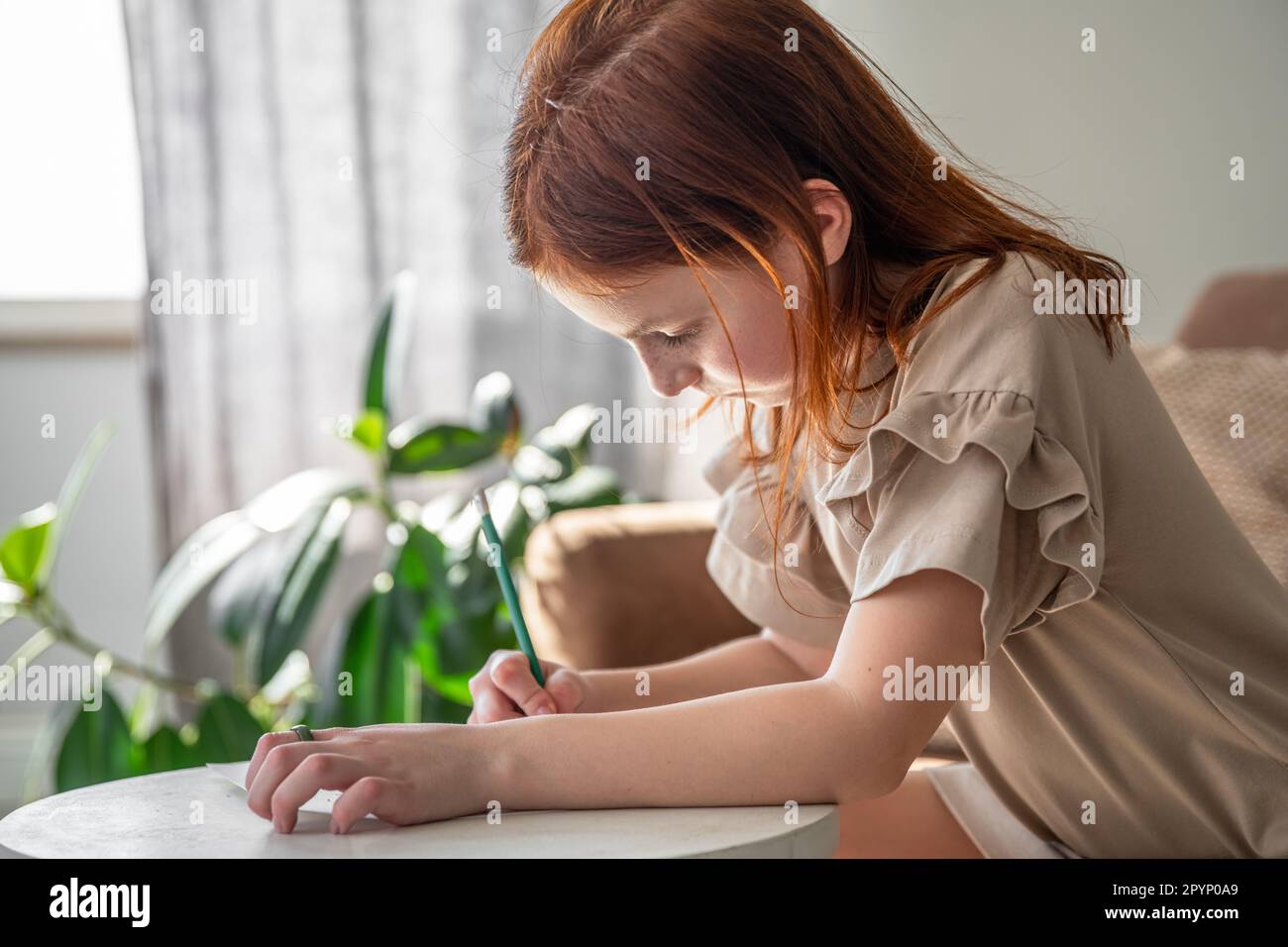 cute little preteen girl drawing with pen while sitting at desk at home, beautiful female child ...