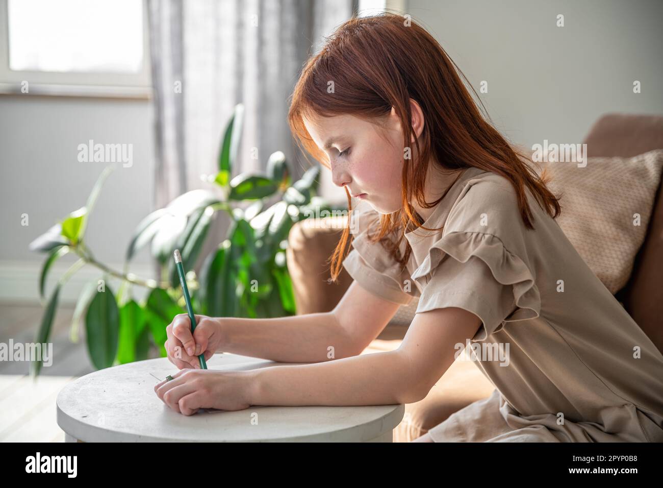 cute little preteen girl drawing with pen while sitting at desk at home, beautiful female child ...