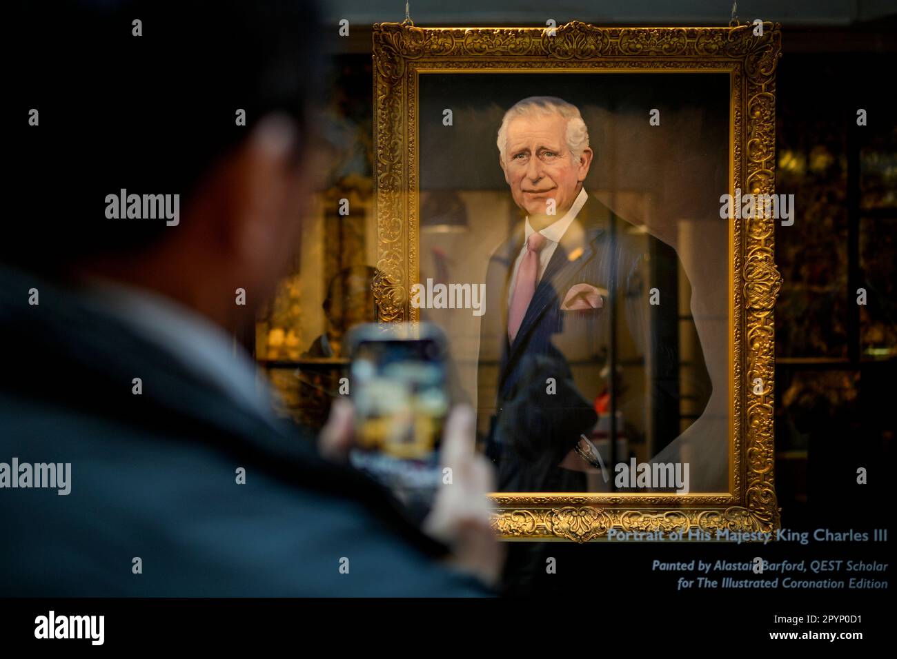 A man takes a picture of a portrait of King Charles III painted by ...