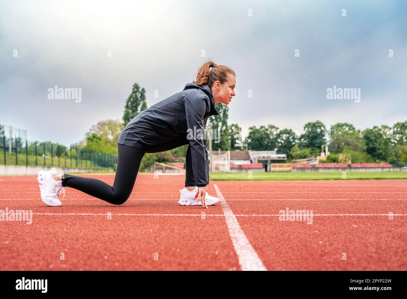 Young woman runner in start position on running track while work out ...