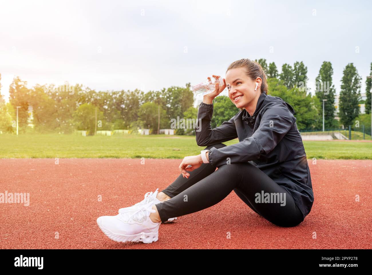 Athletic young woman runner sitting on running track resting after ...