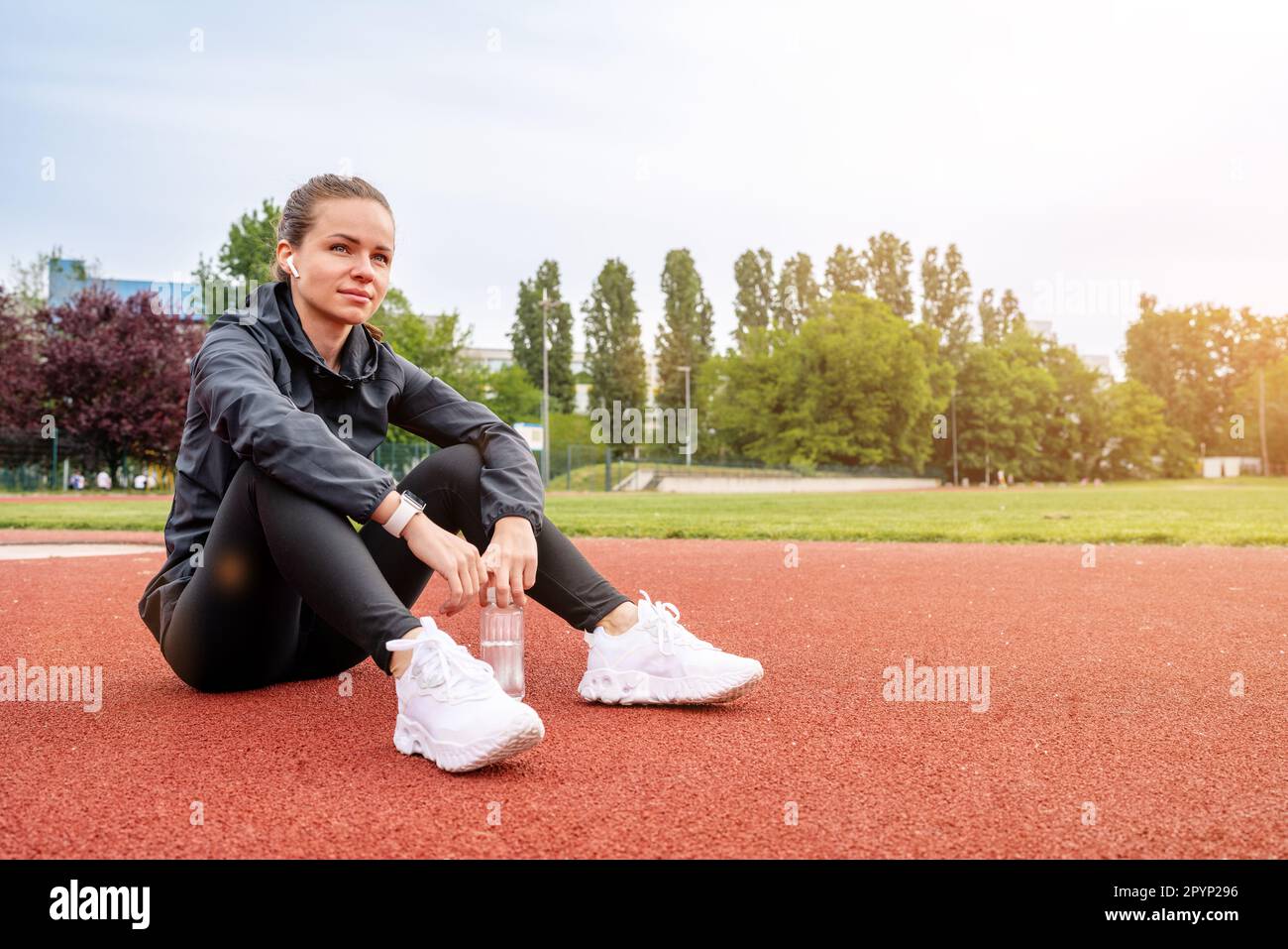 Athletic woman runner sitting on running track and resting after ...
