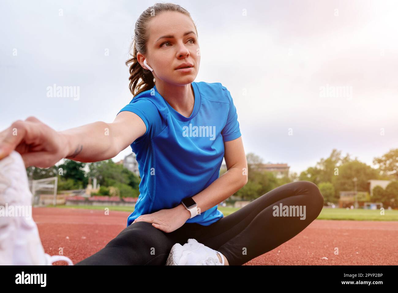 Athlete woman with wireless earphones doing stretching exercise after ...