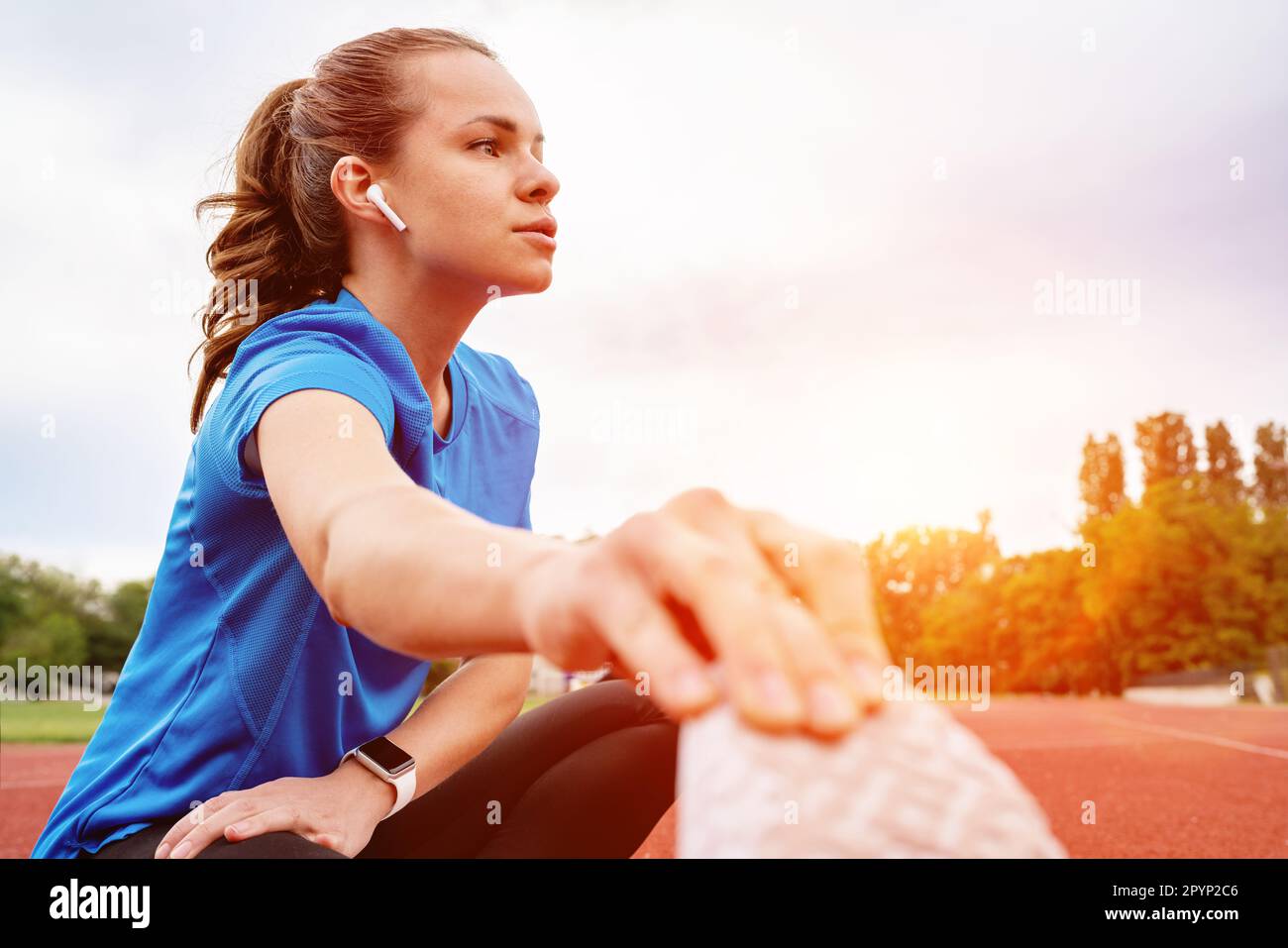 Athlete woman with wireless earphones doing stretching exercise after ...