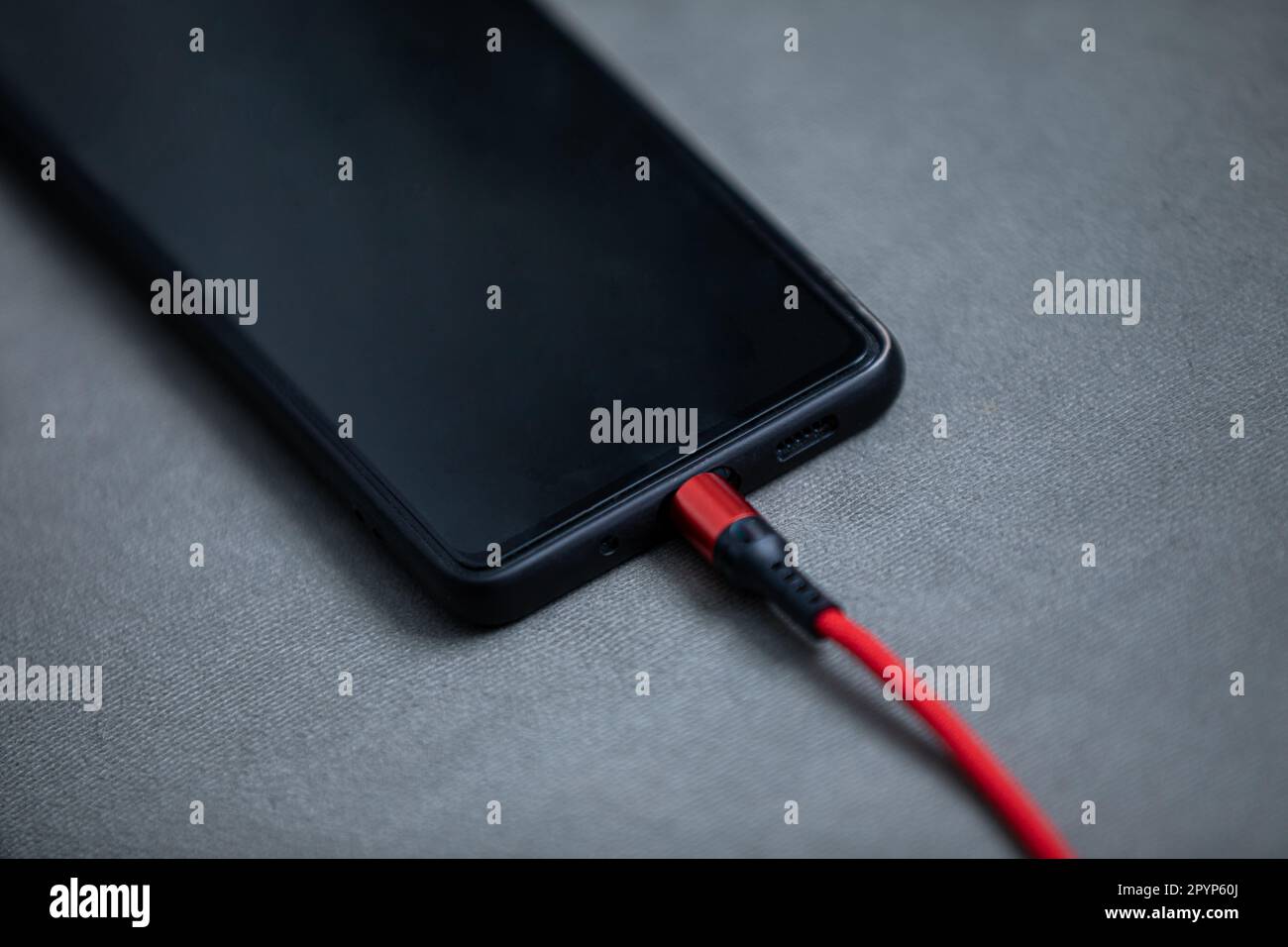 A black smartphone is lying and is connected to the power supply with a ...
