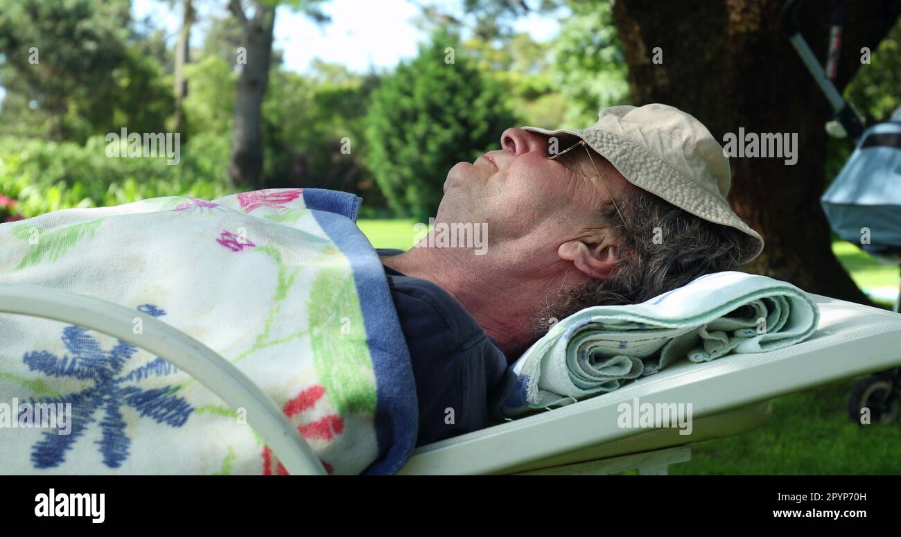 Man in 70s asleep outside. Older man with face covered with had napping ...