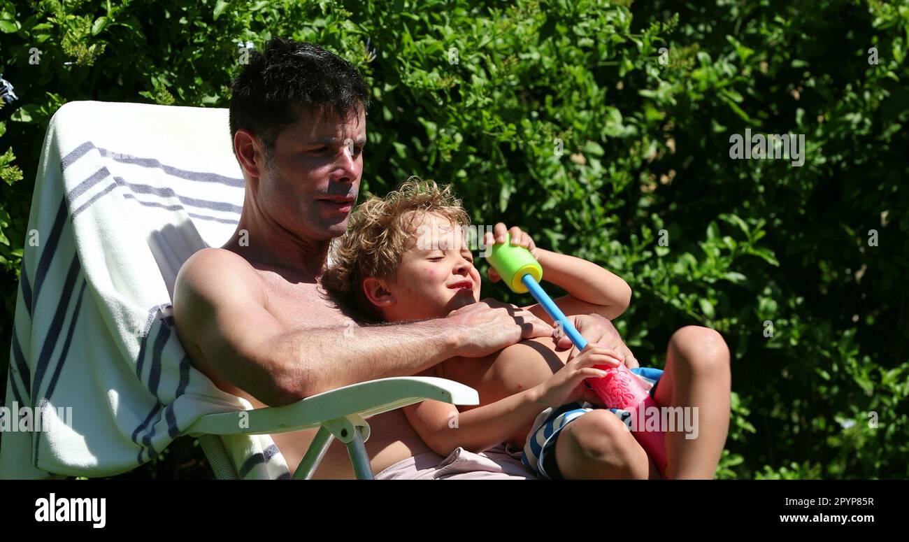 Father and child son interaction outside in sunlight. Toddler lying and ...